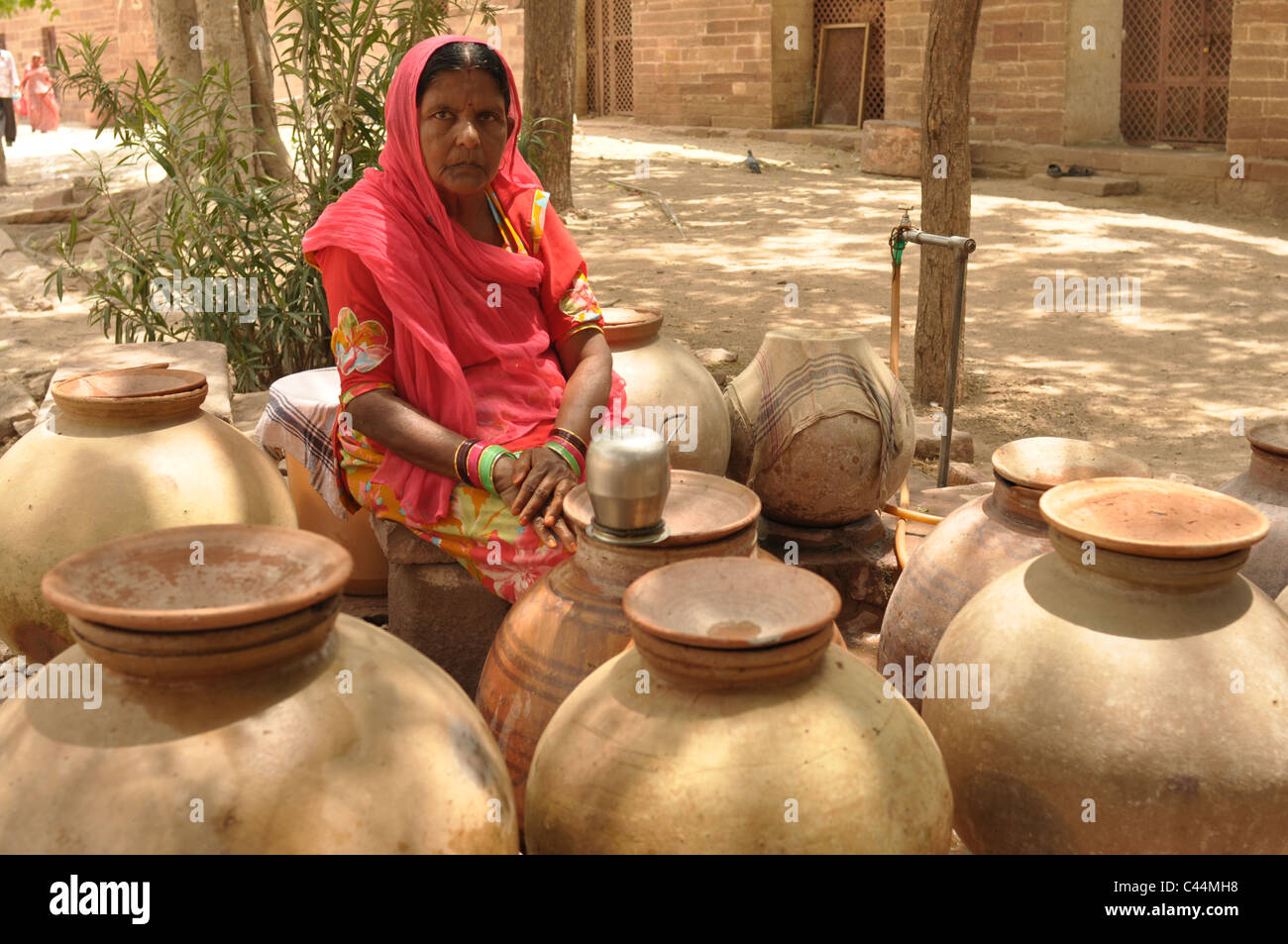 An old lady sitting with water containers around to serve water on a ...