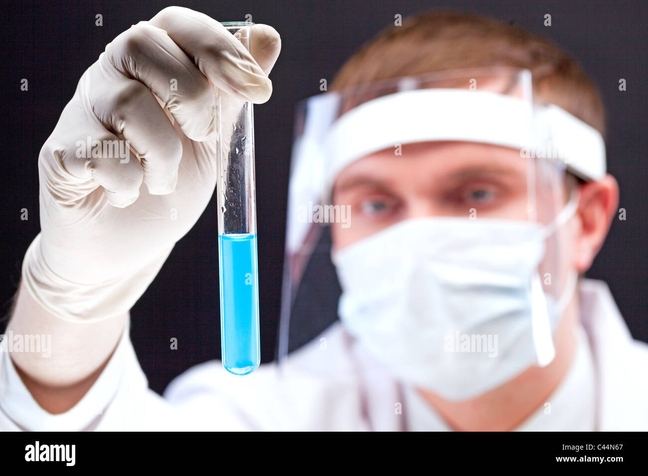 Laboratory worker looking at flask with blue liquid through transparent ...