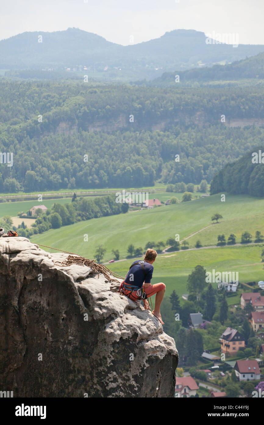 Rock climber sitting at the edge, village seen in distance Stock Photo ...