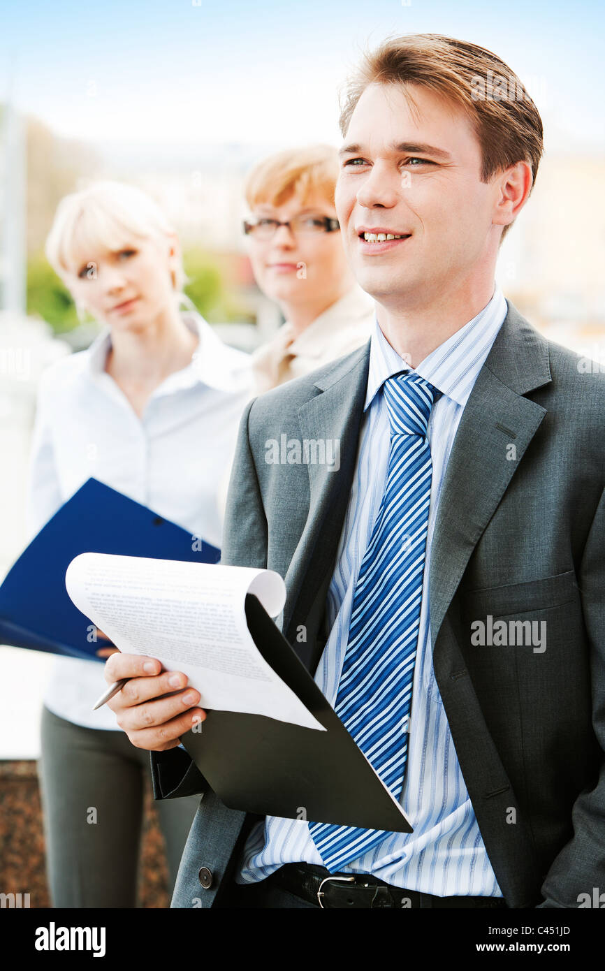 Portrait of serious boss holding pen over paper with young ladies at ...