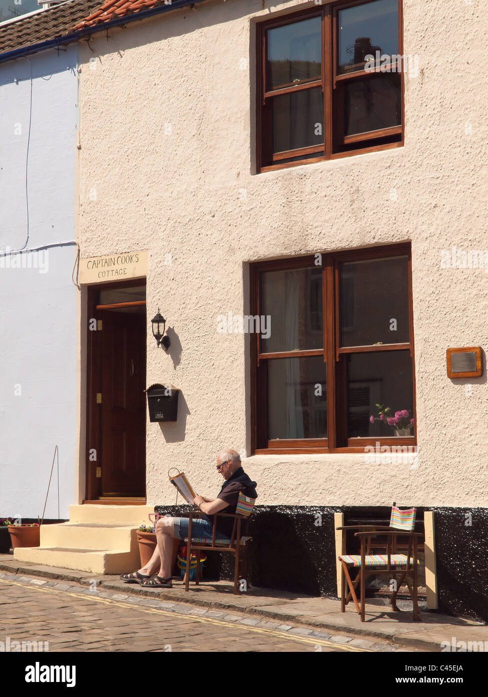 A man sitting outside Captain Cook's Cottage in Staithes North ...
