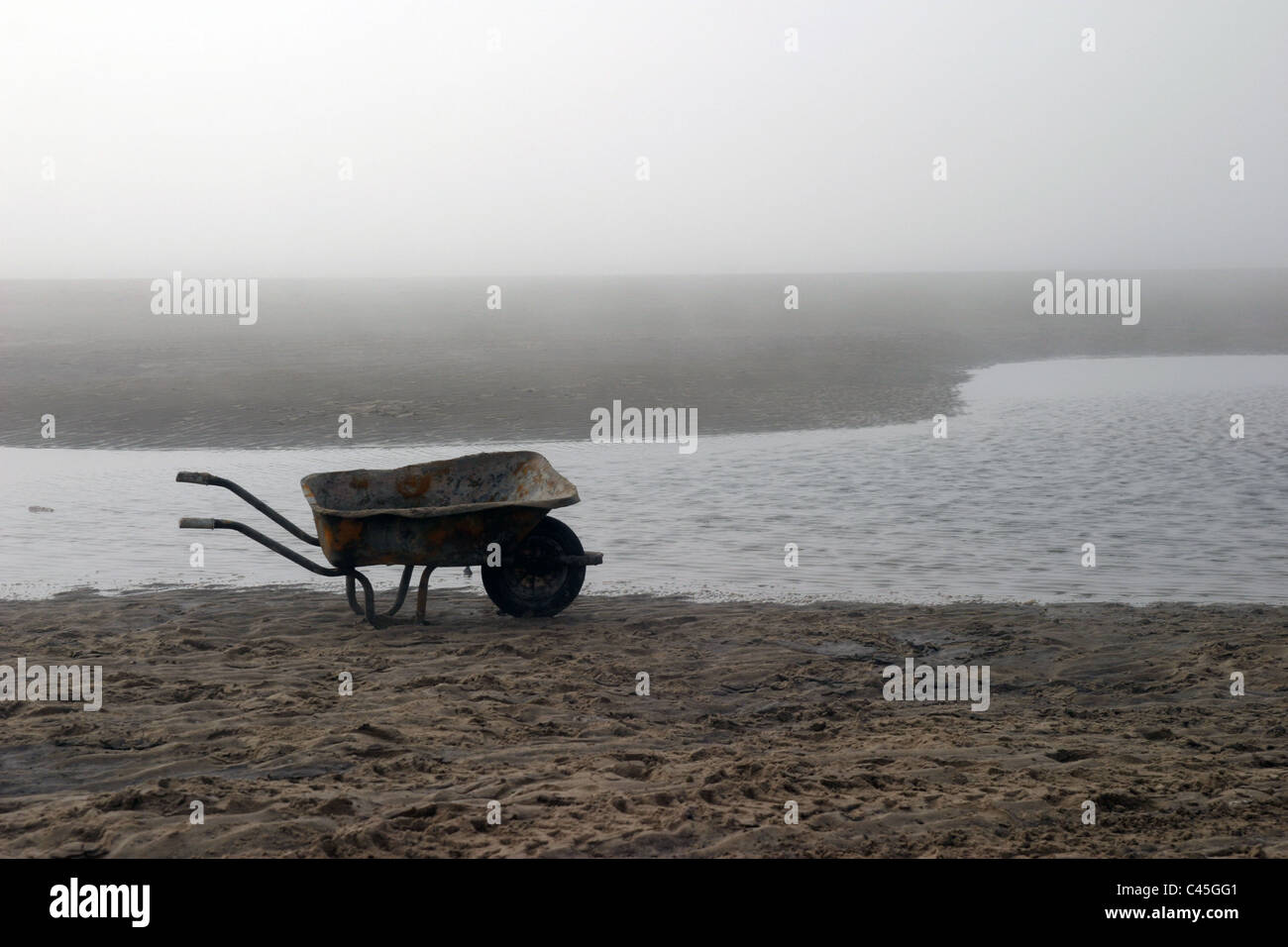 The image shows an old abandoned wheelbarrow on the foggy beach in ...