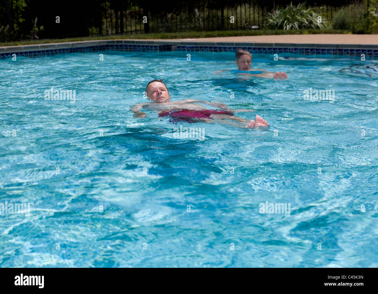 Baby boomer couple floating in a backyard swimming pool on a hot ...