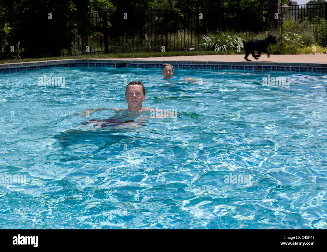 Baby boomer couple floating in a backyard swimming pool on a hot ...