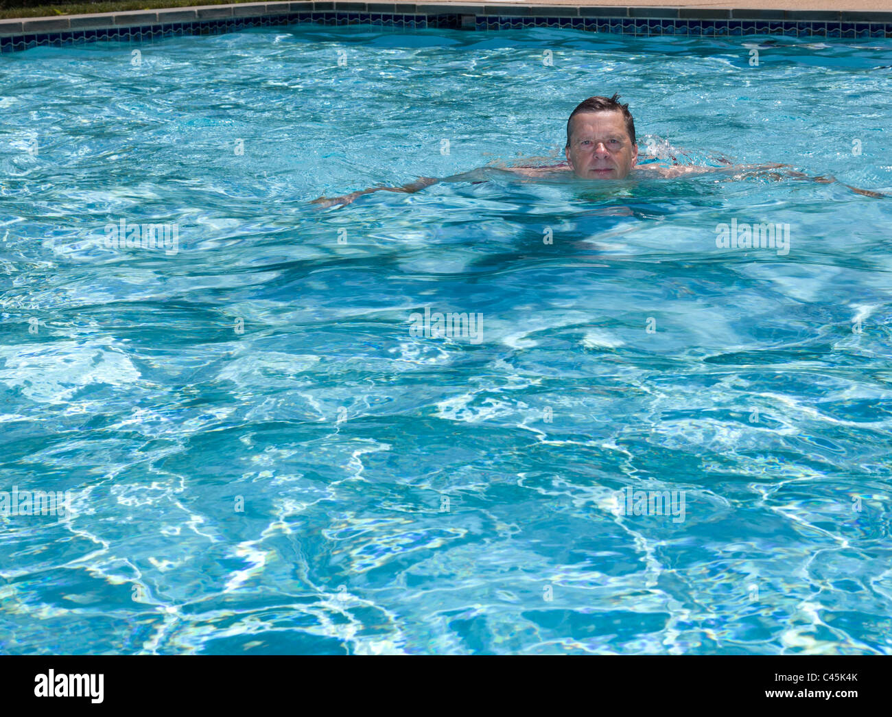 Baby boomer male floating in a backyard swimming pool on a hot summers ...