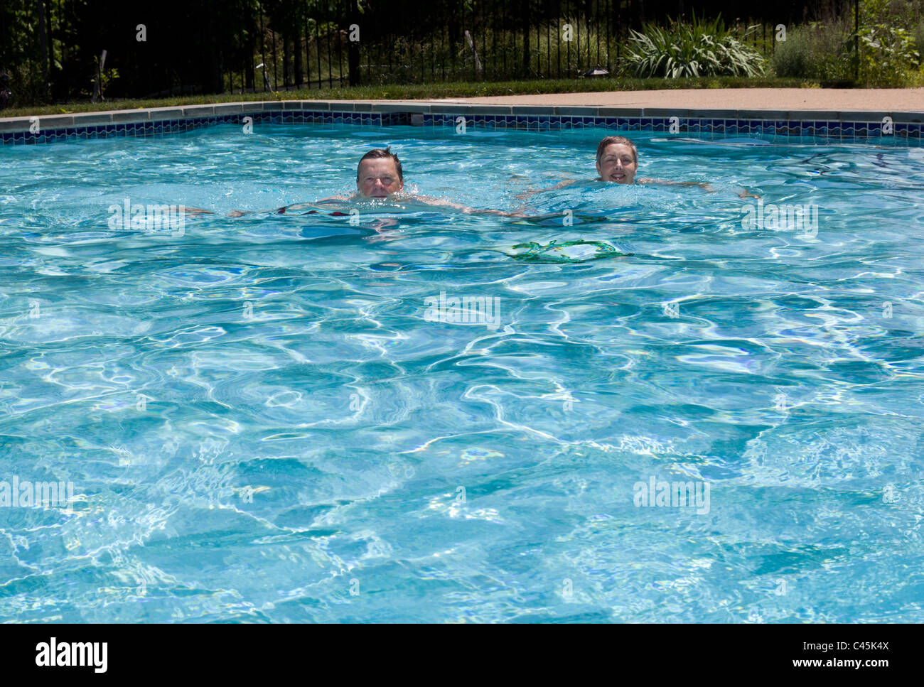 Baby boomer couple floating in a backyard swimming pool on a hot ...