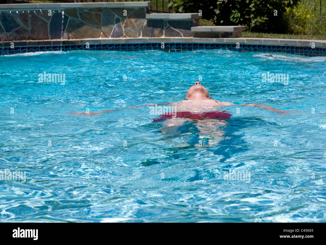 Baby boomer male floating in a backyard swimming pool on a hot summers ...