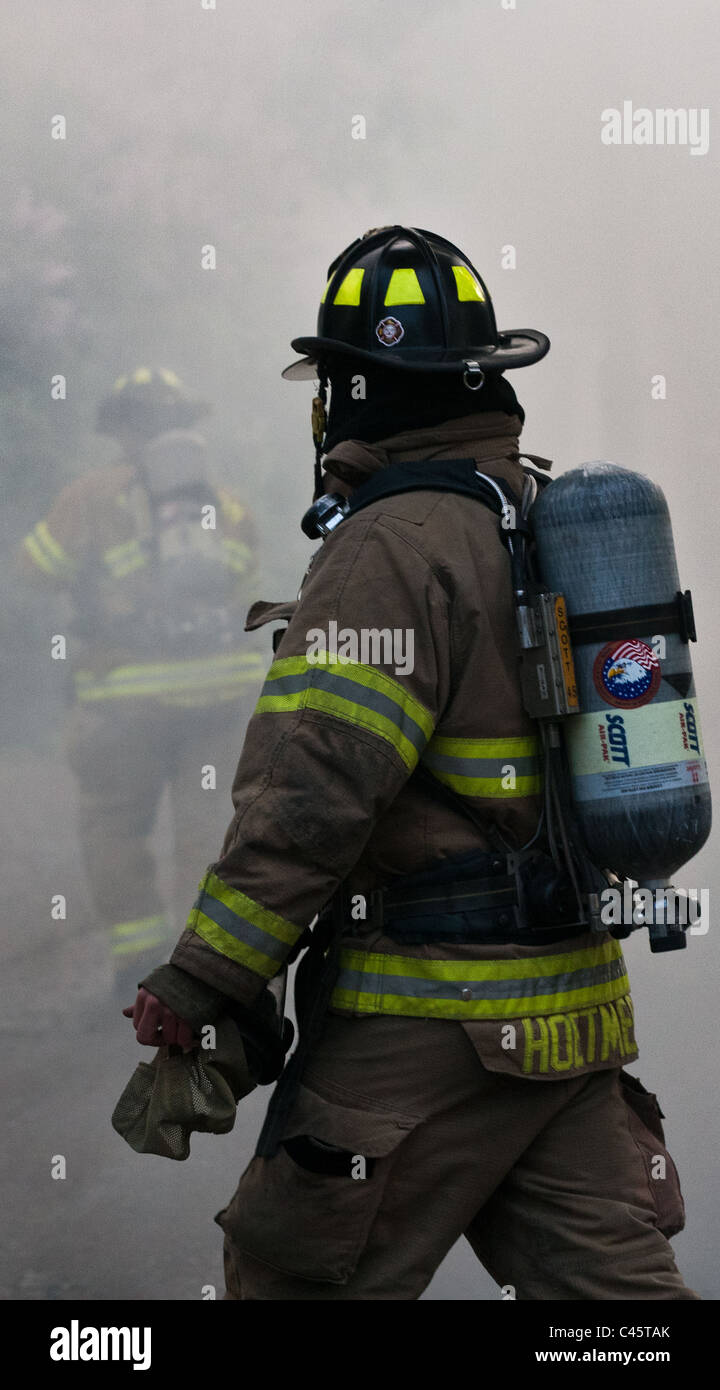 Fireman in smoke of house fire in full protective equipment. A second ...