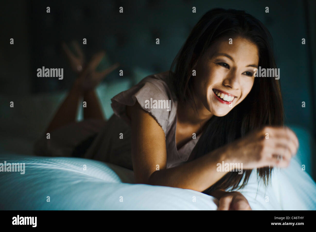 A woman laying across a bed laughs Stock Photo - Alamy