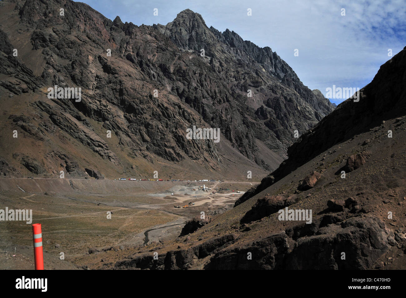 Mountain valley view lorries climbing incline below dark scree cliffs ...