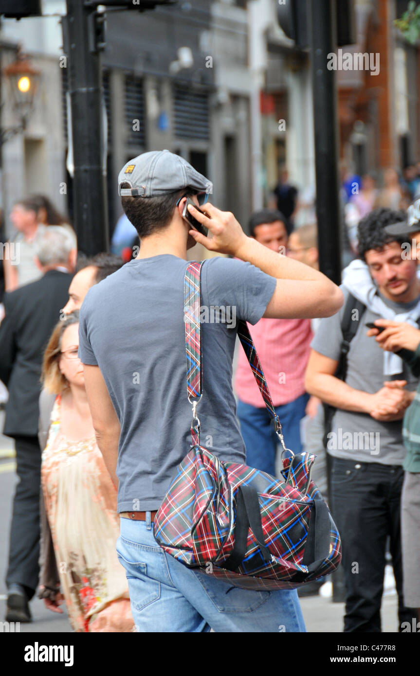 Young London man wearing cap with shoulder bag talking on mobile phone ...