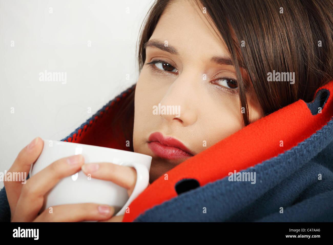 Young woman caught cold, wrapped up in blanket, drinking something hot ...