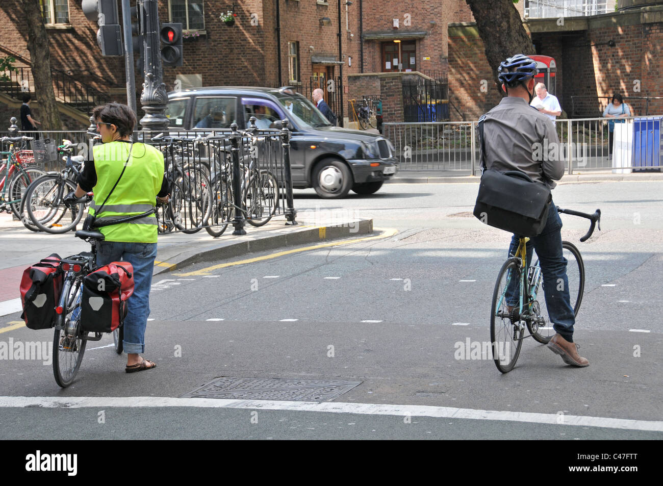 Two cyclists waiting at traffic lights London black cab road junction ...