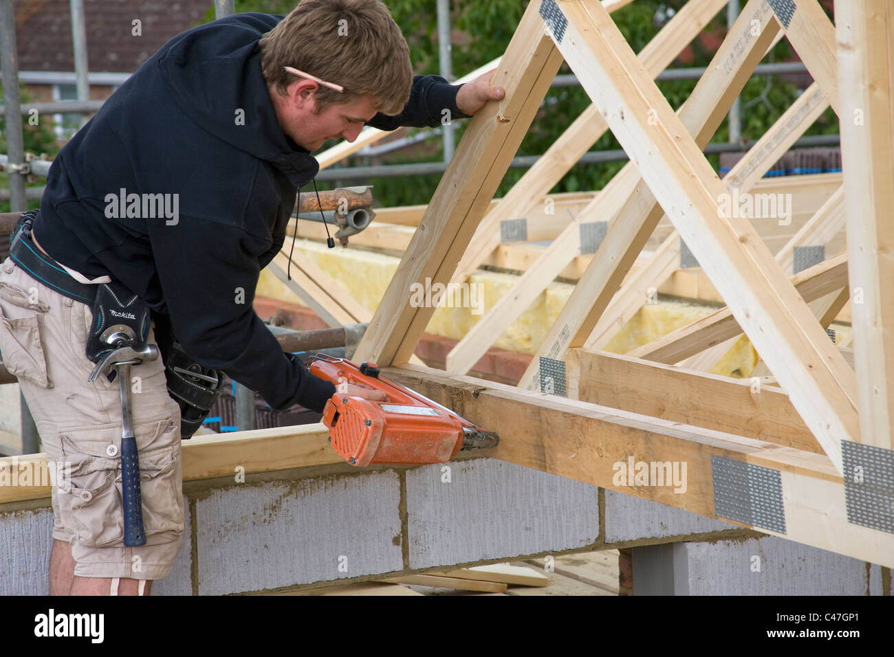 Carpenter using a nail gun to join roof trusses Stock Photo - Alamy