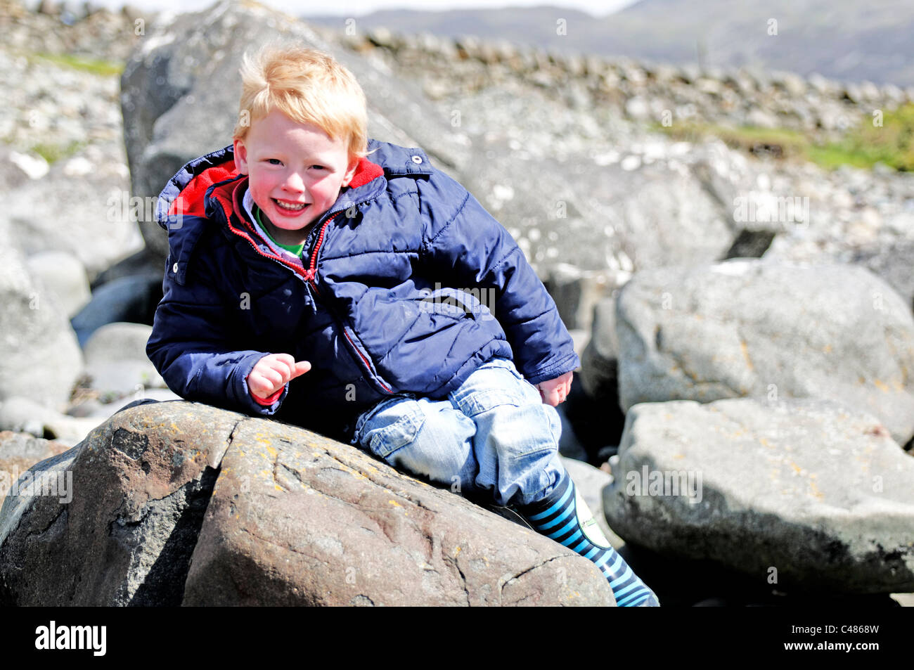 A young boy sat on a boulder on the beach Stock Photo - Alamy