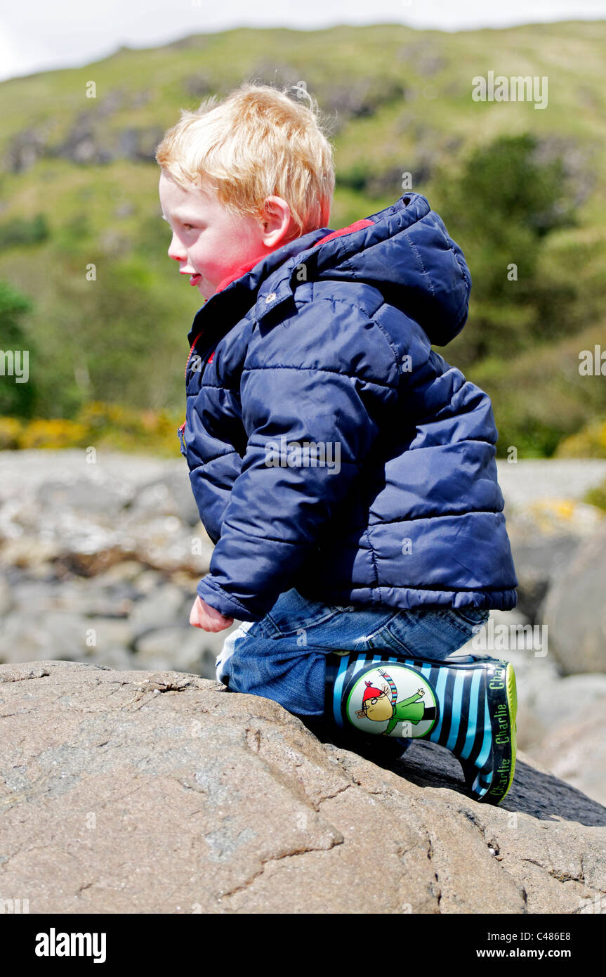 A young boy sat on a boulder on the beach Stock Photo - Alamy