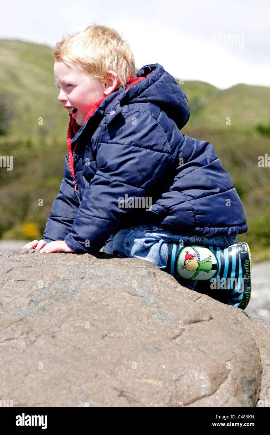 A young boy sat on a boulder on the beach Stock Photo - Alamy