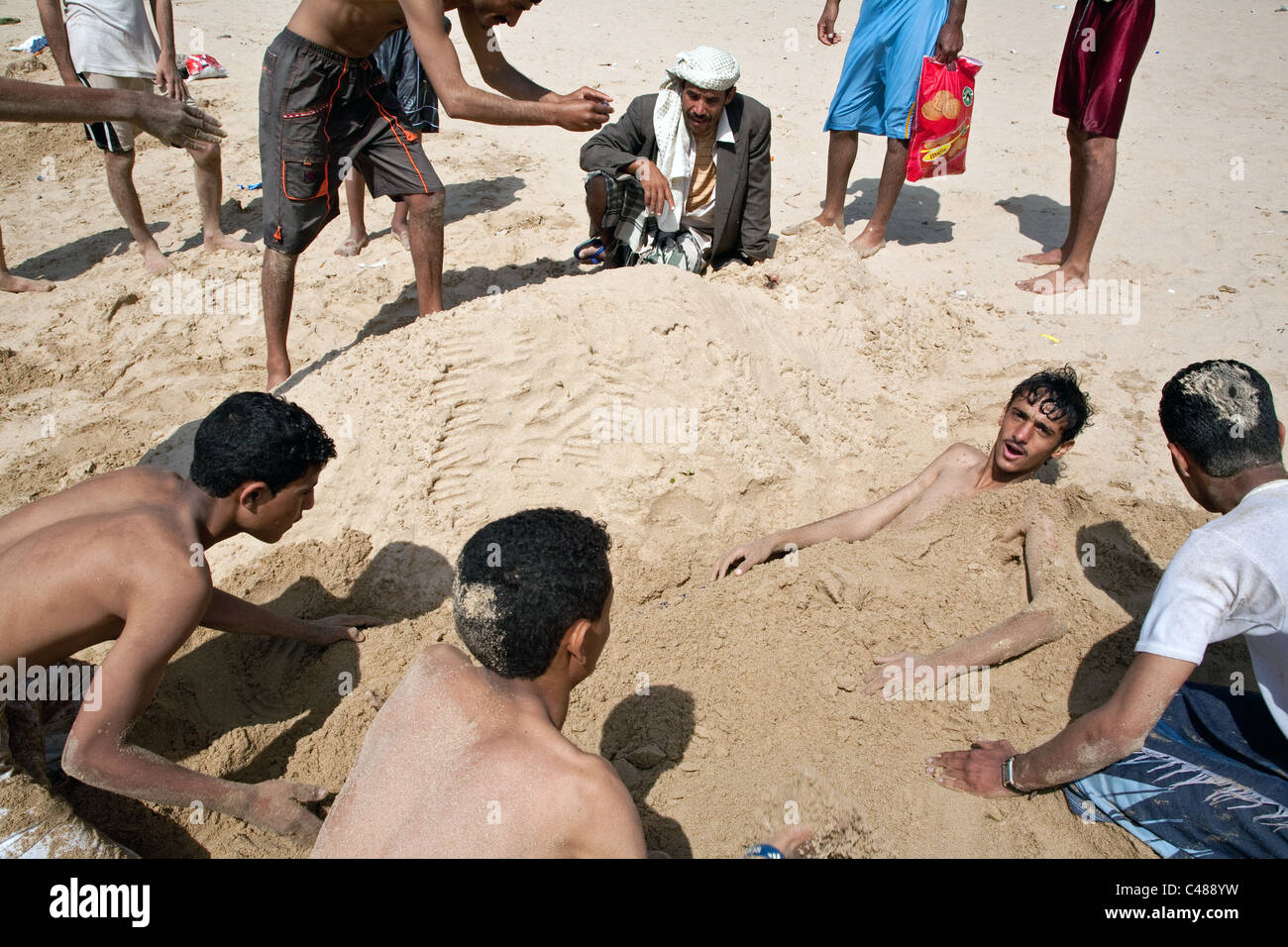 People playing in the sand and burying other for fun on the beach on ...