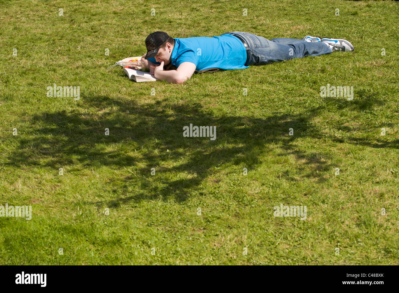 Man Reading Book Lying On Grass With Shadow Of Tree At Hay Festival
