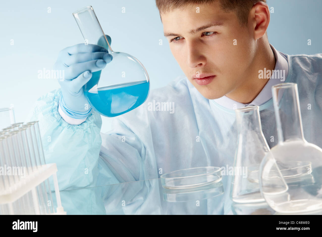 Serious clinician looking at flask with blue liquid in laboratory Stock ...