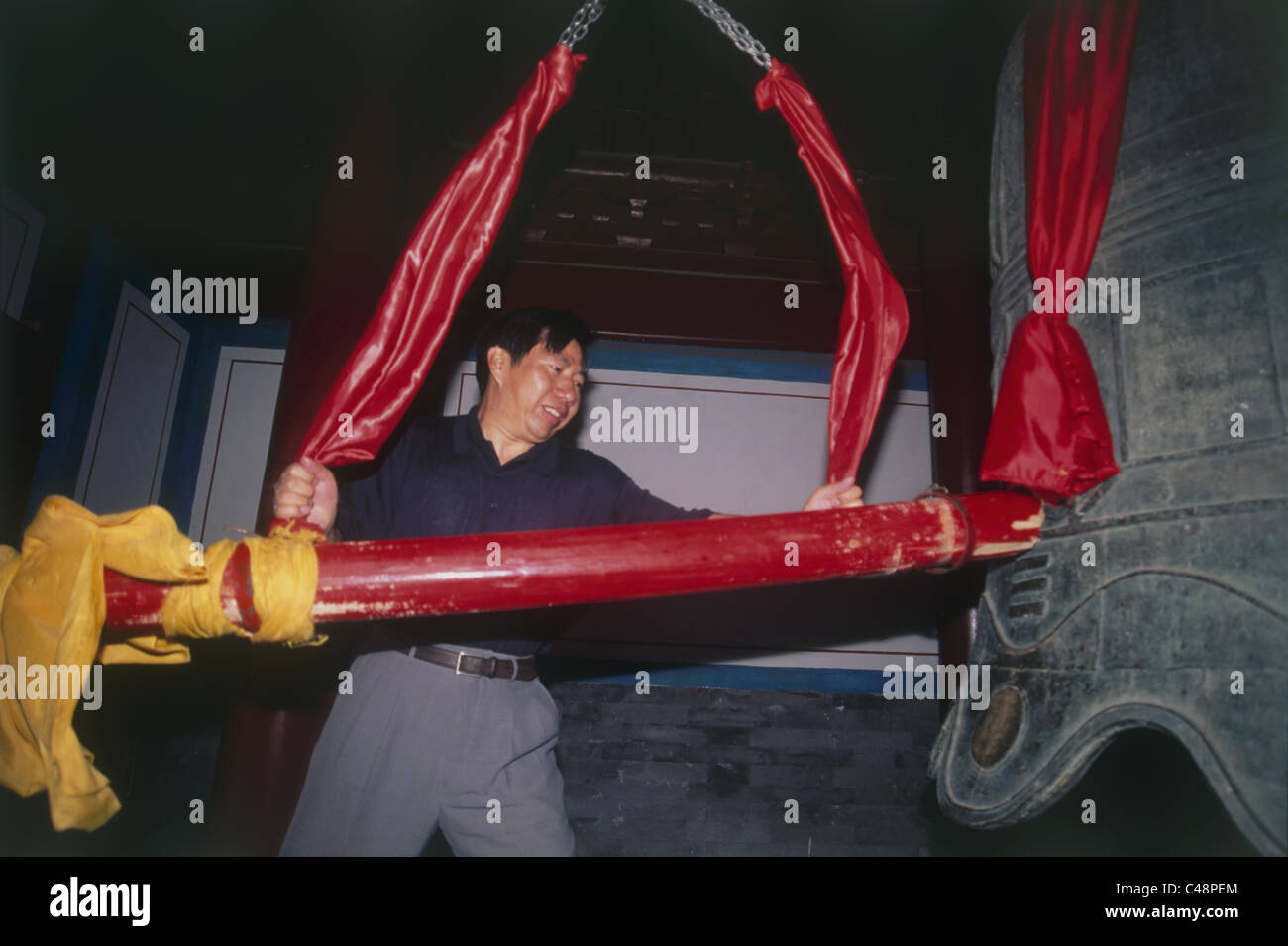 Photograph of a Chinese man striking a large bell in a shrine in ...