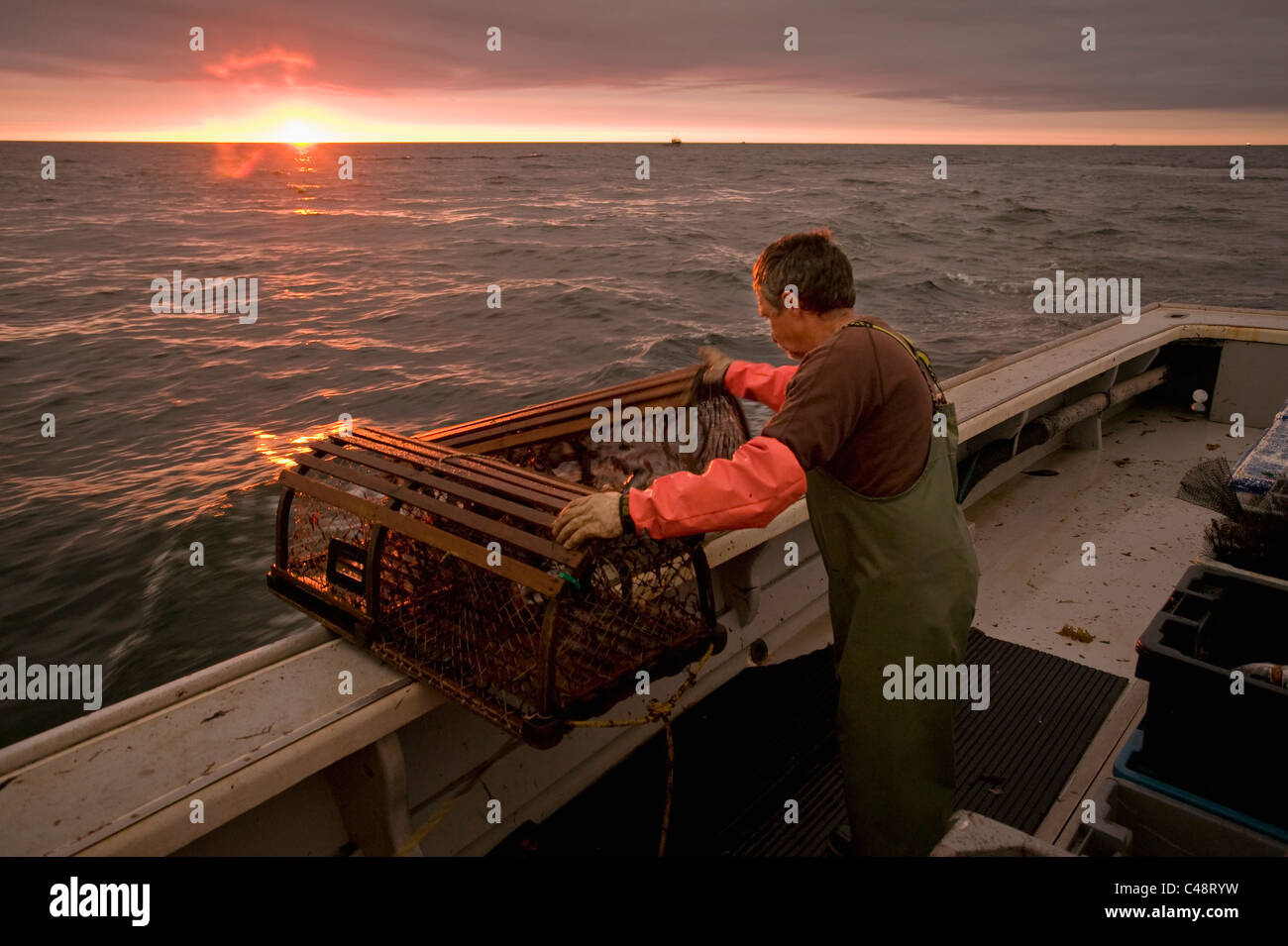 A fisherman sets a lobster trap as the sun breaks over the horizon off ...