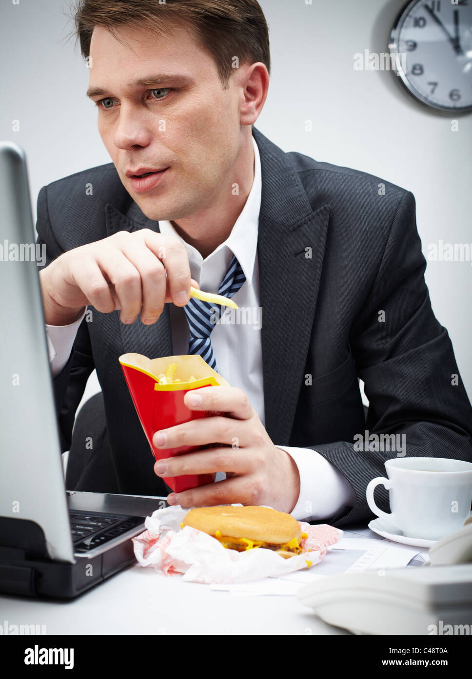 Portrait of serious businessman looking at laptop screen while eating ...