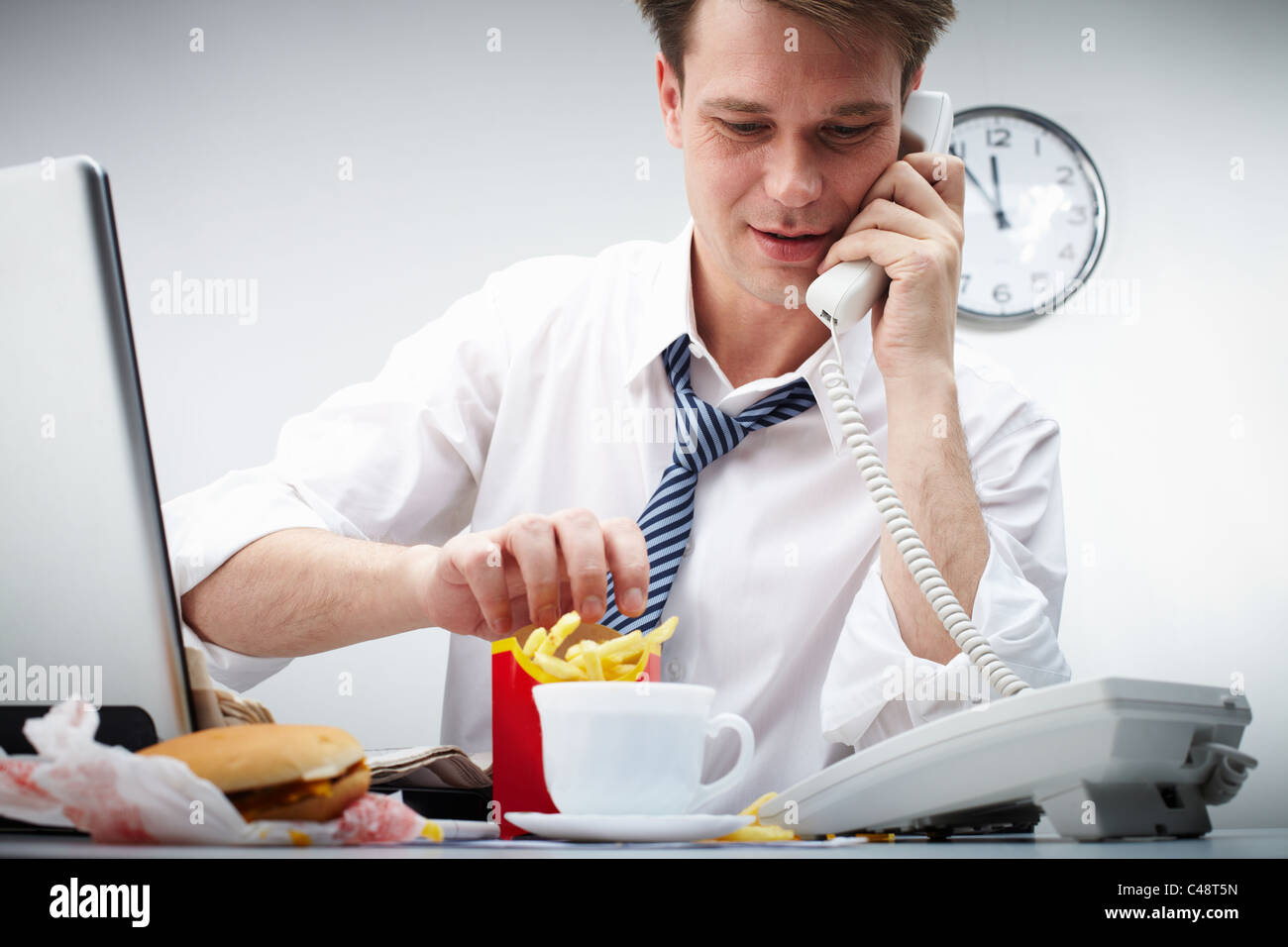 Portrait of modern businessman speaking by the phone while eating fries ...