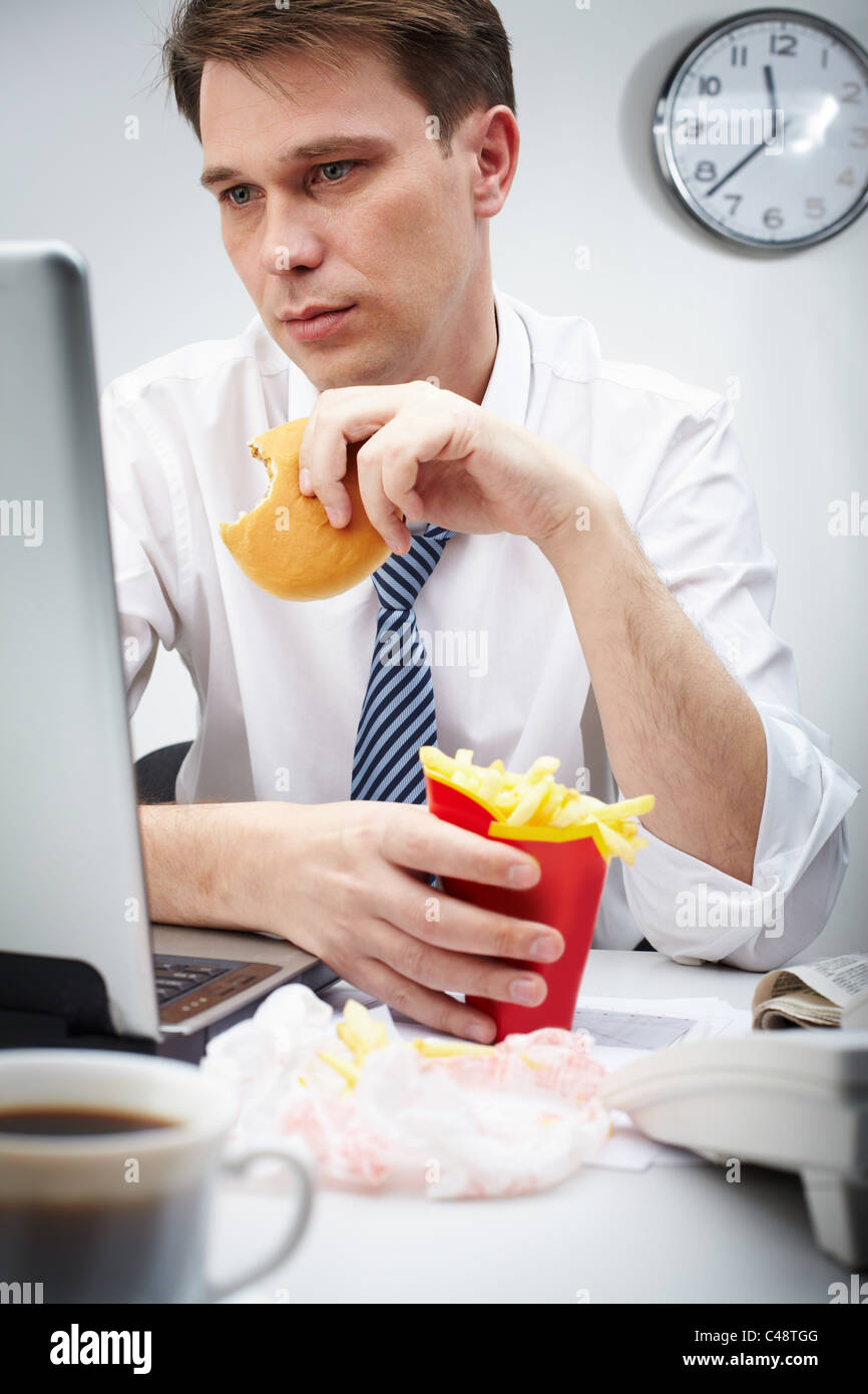 Portrait of serious businessman looking at laptop screen while eating ...