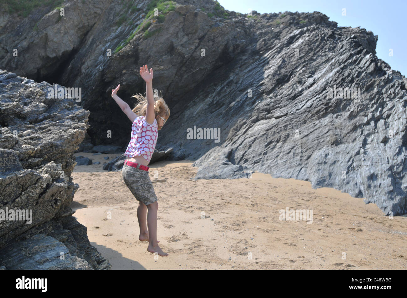 An 8 year old girl jumping from a rock on a Cornish beach Stock Photo ...