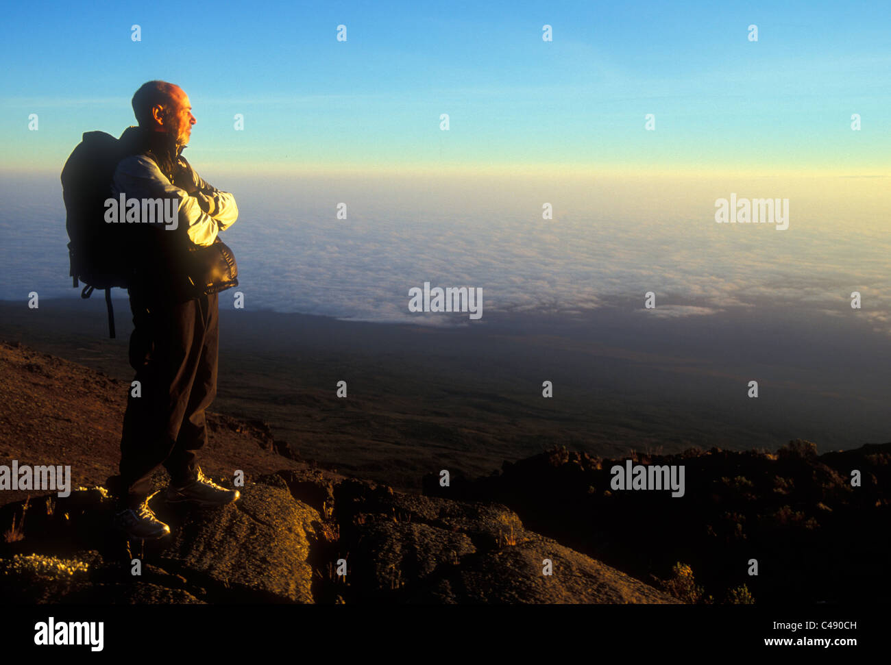 A man stands alone at sunrise as he looks down to the Tanzanian plains ...