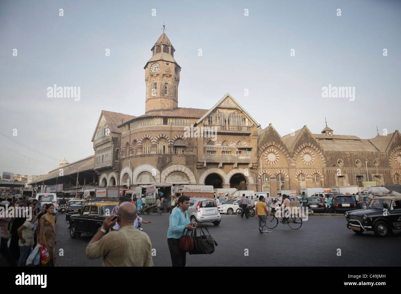 People walk along a crowded street in india with an ornate building in ...