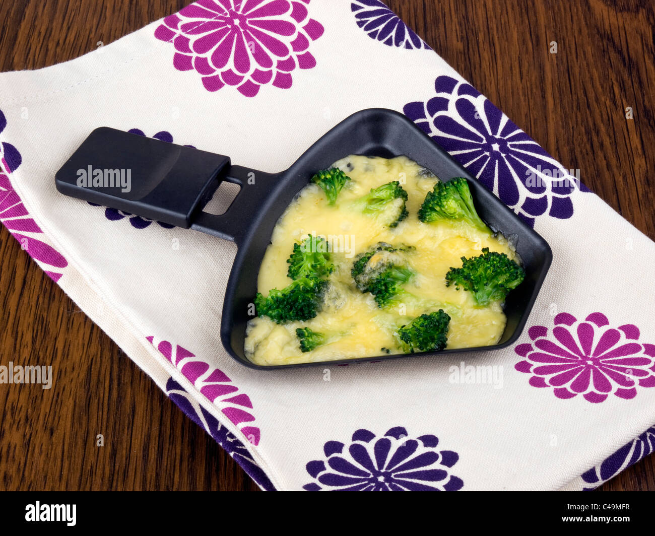 Raclette pan with cheese and broccoli on colorful napkin Stock Photo ...