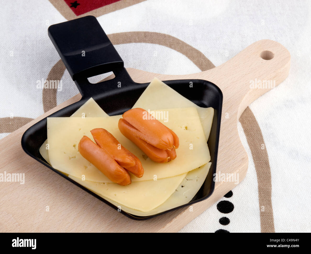 Raclette pan with cheese and cocktail sausages on chopping board Stock ...
