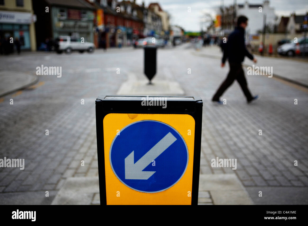 A man crosses a road in front of a keep left bollard on a UK street ...