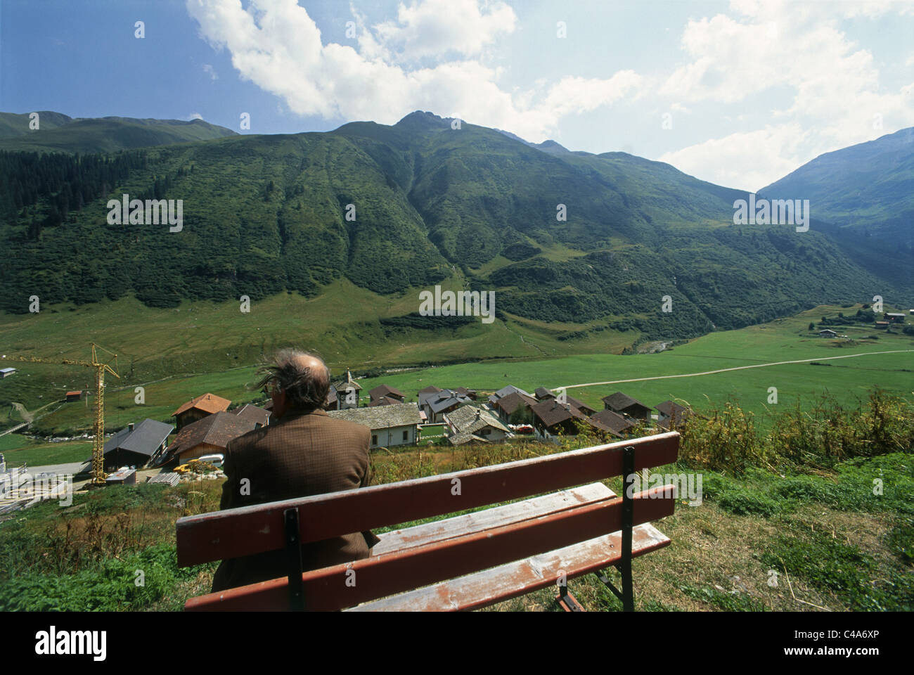 Photograph of a swiss man sitting on a bench and looking at his village ...