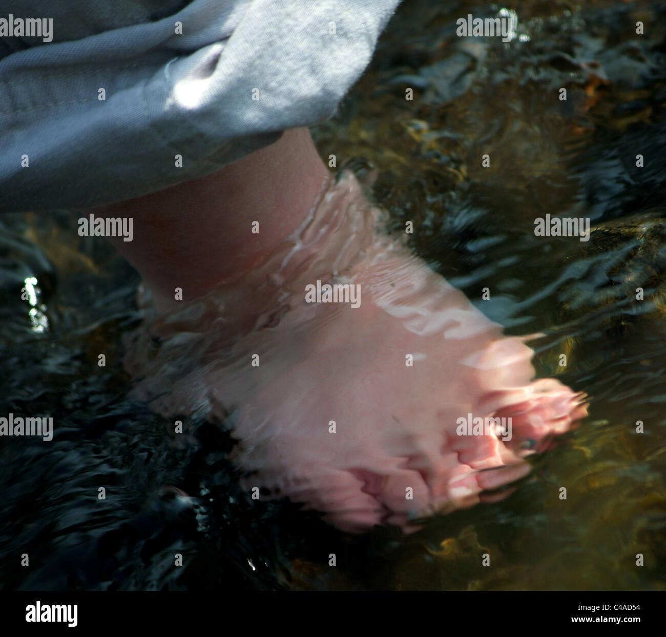 A young toddler child with wet feet after paddling in a river of moving ...