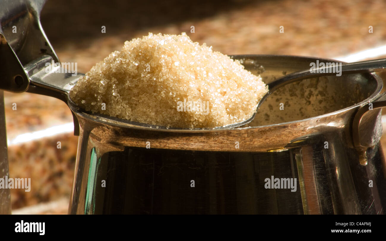 Close-up of spoon with natural brown sugar over a stainless sugar bowl ...