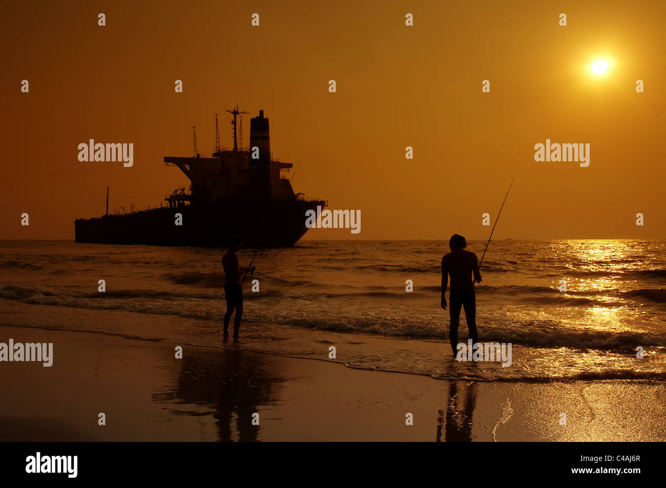 Two men fishing on Candolim Beach, Goa with the wreck of the River ...