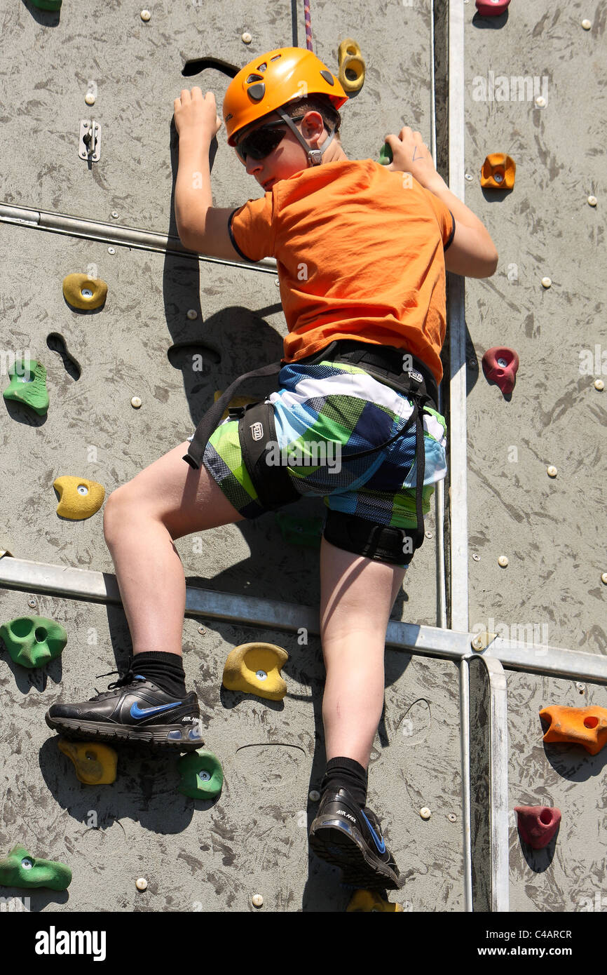 A young boy learning how to rock climb on a climbing wall outside in ...