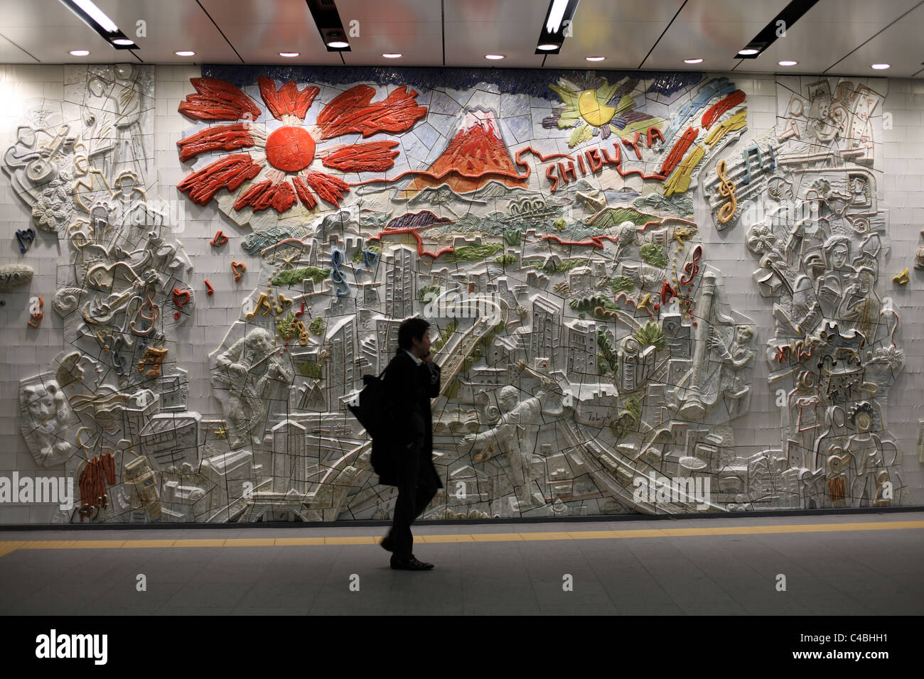Man talking on mobile phone walks past a wall mural at Shibuya metro ...
