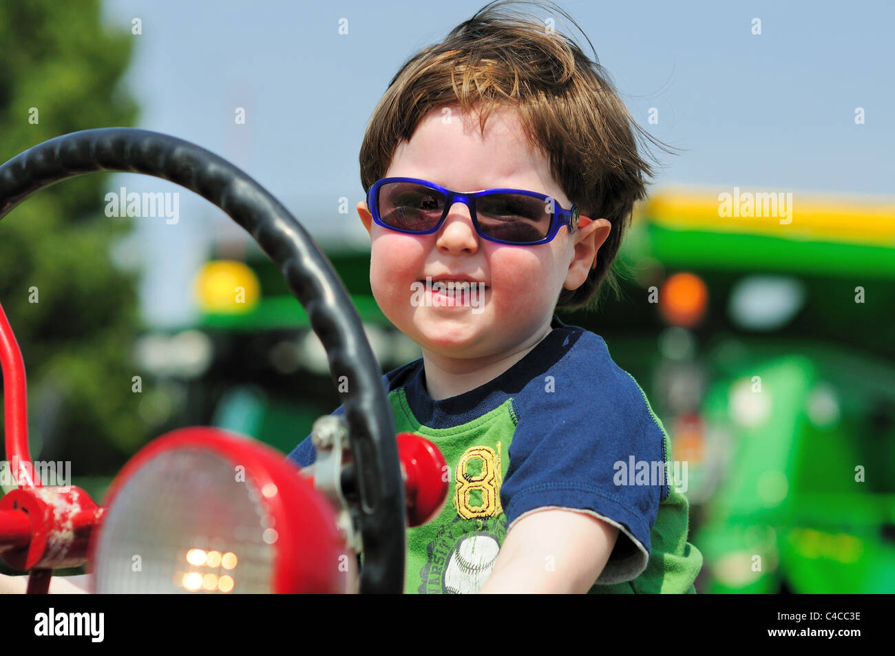 Little boy smiles as he enjoys an imaginary ride on a tractor on ...