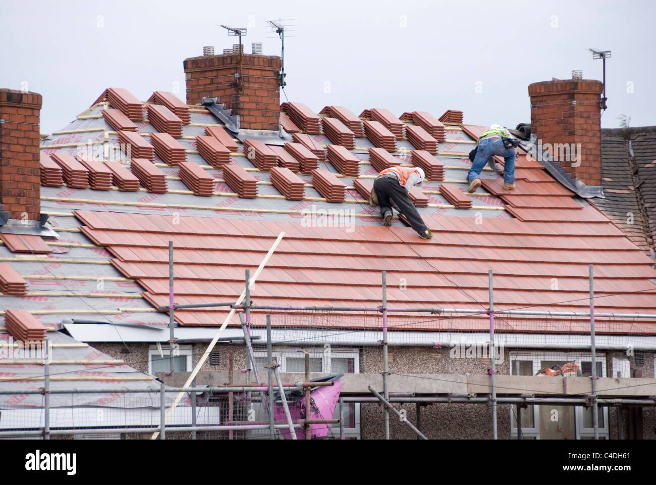 Two Men on Roof of House Laying New Roof Tiles on Three Neighbouring ...
