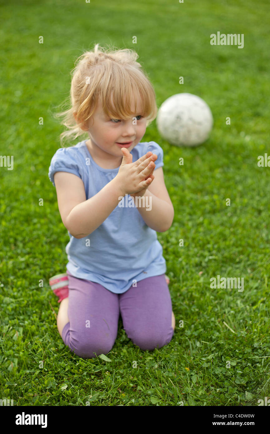 Child clapping hands while playing in the grass, soccer ball near Stock ...