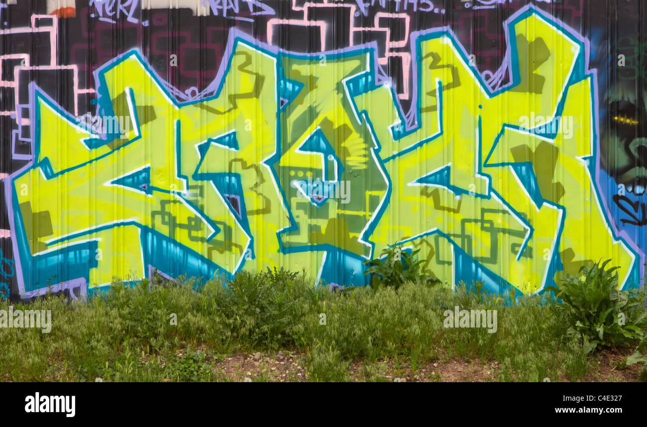 Yellow and blue graffiti painted on a corrugated steel wall with grass ...