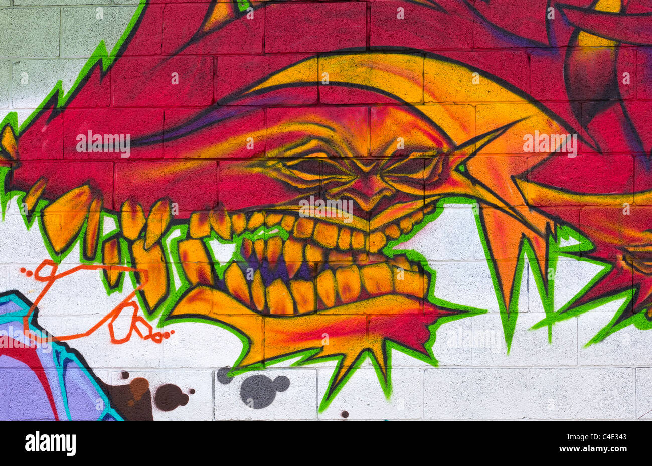 An evil face painted in a graffiti image on a white painted block wall ...