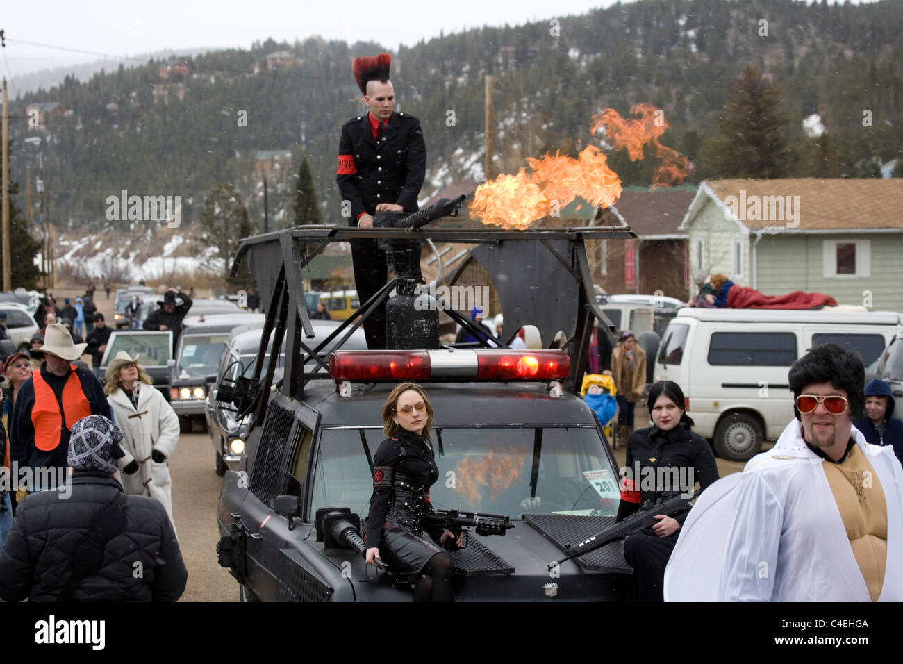 A man dressed as a punk rocker stands atop a hearse with a lit flame ...