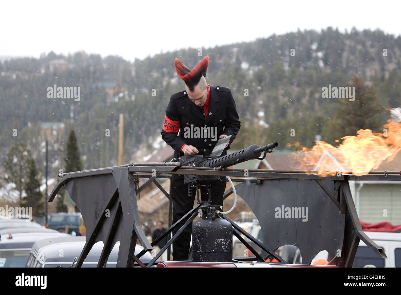 A man dressed as a punk rocker stands atop a hearse with a lit flame ...