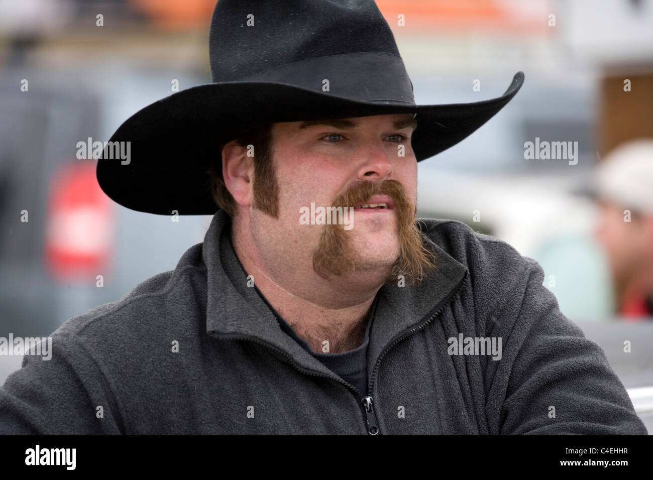 A man in a wide brim black cowboy hat surveys the crowd during a parade ...