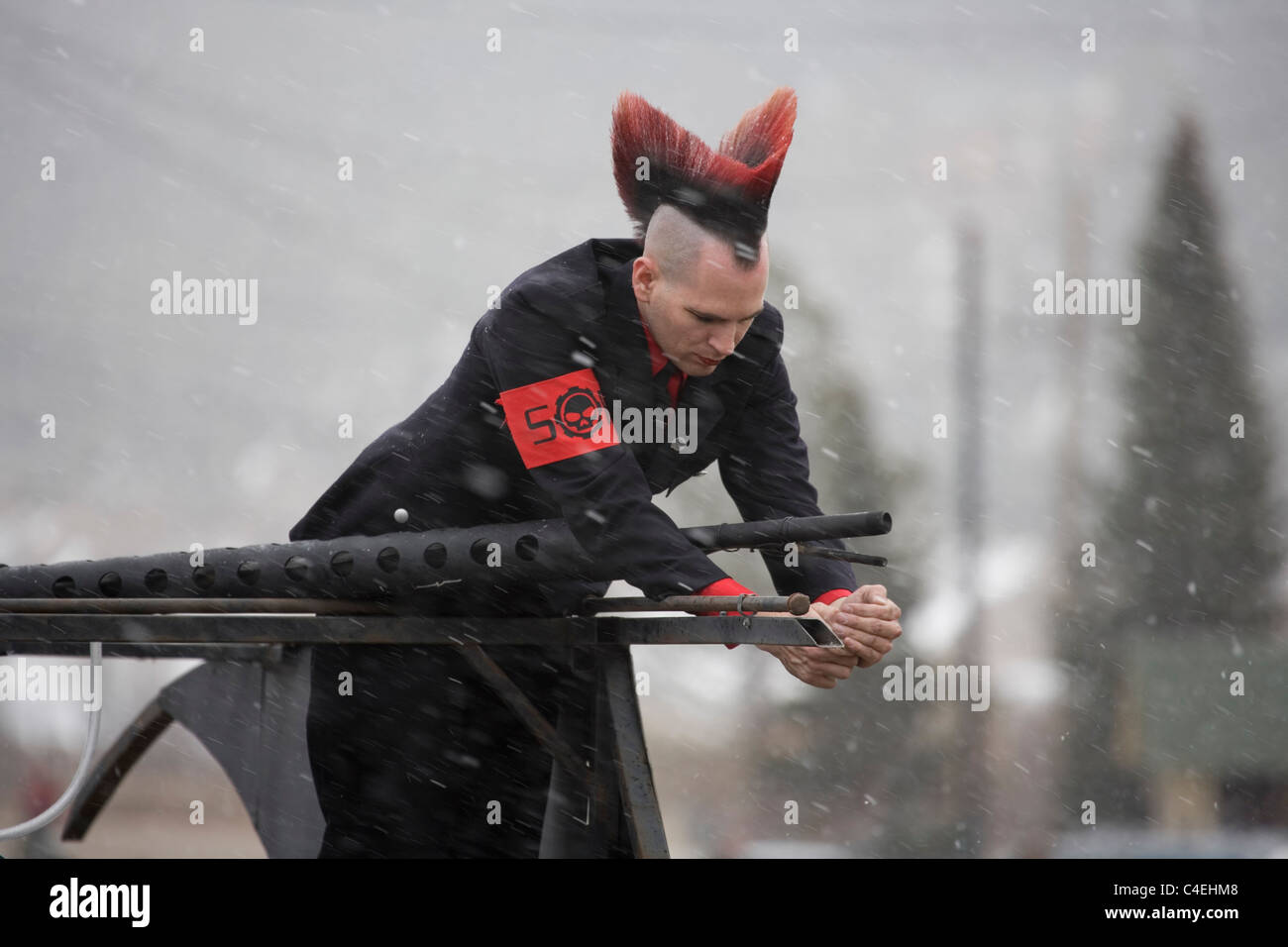 A man dressed as a punk rocker stands atop a hearse lighting a flame ...